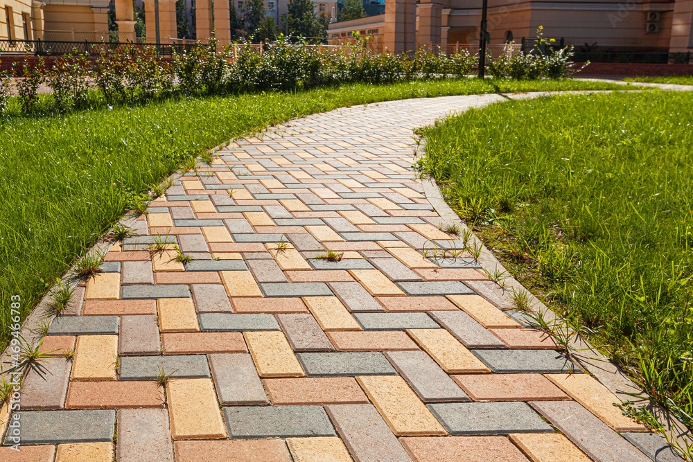 The pedestrian path is paved with multi-colored paving stones. Grass ...