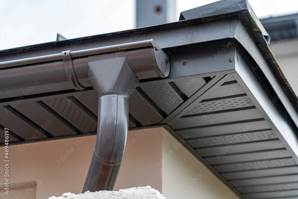 Corner of house with new gray metal tile roof and rain gutter. Metallic ...