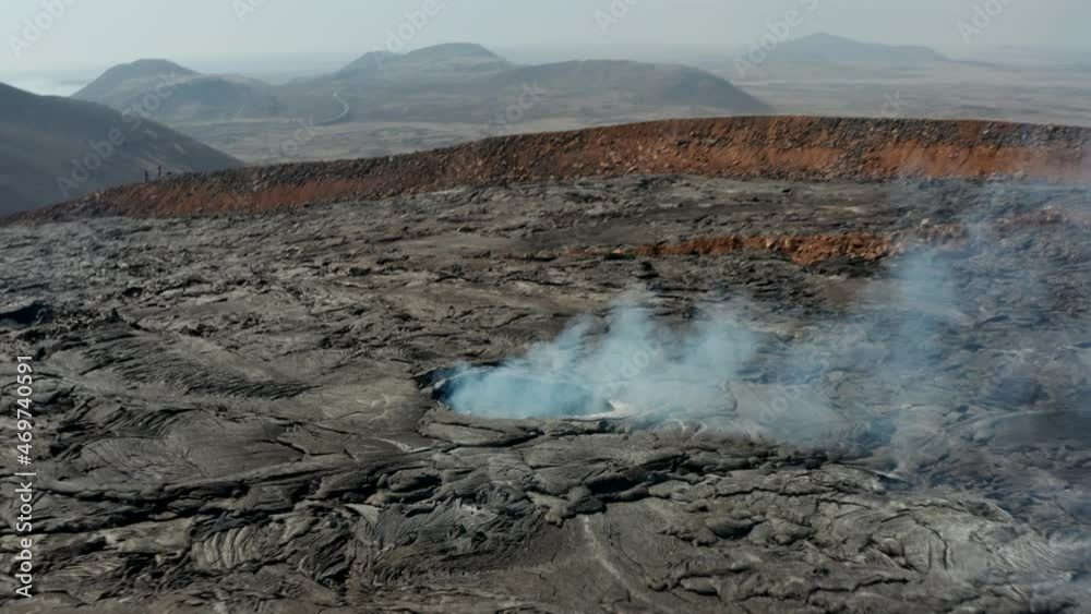 Fly over large hole in cooling lava layer emitting smoke. Volcanic ...