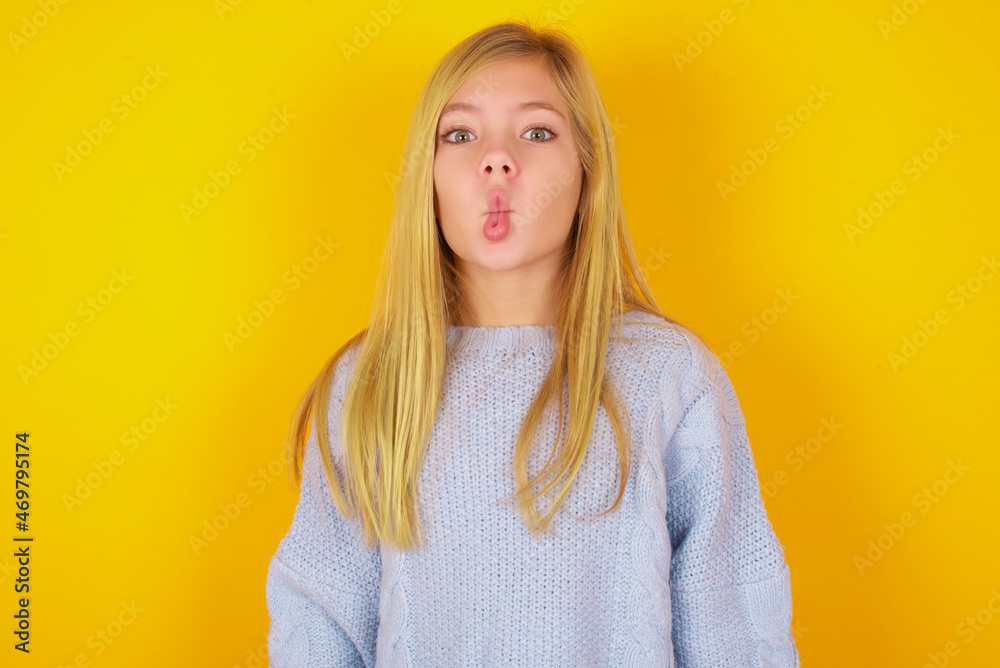 caucasian kid girl wearing blue knitted sweater over yellow background ...
