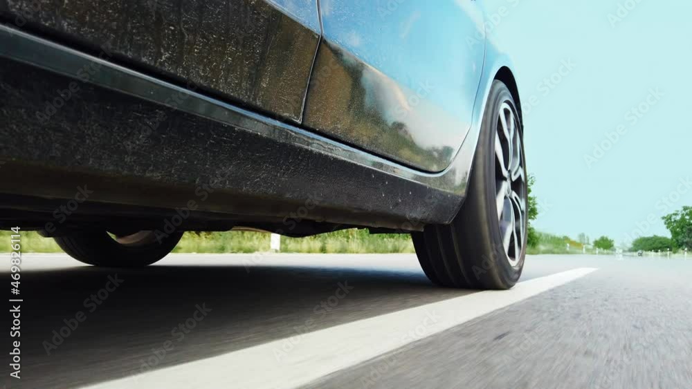 Low angle side view of sport car's tires speeding on the empty road ...