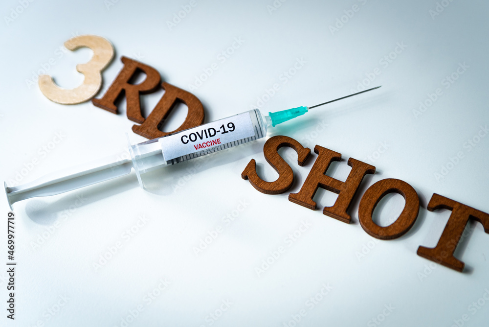 3rd covid vaccine booster shot concept with face mask. Syringe is seen ...