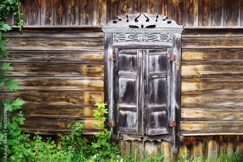 Wooden shuttered window in a rustic log old house in thickets of grass ...