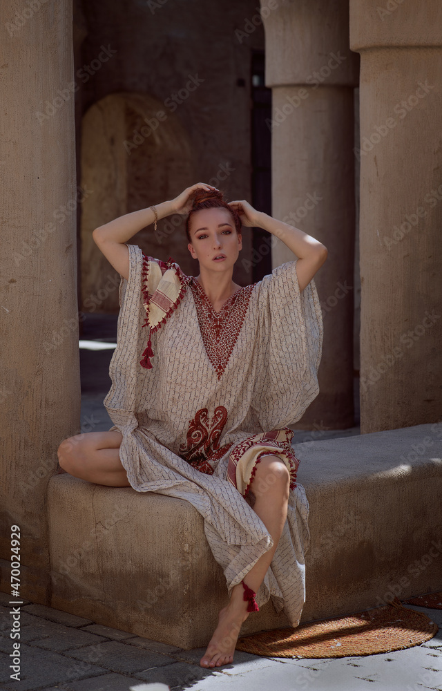 red-haired beautiful girl in Arabic clothes sit against the background ...