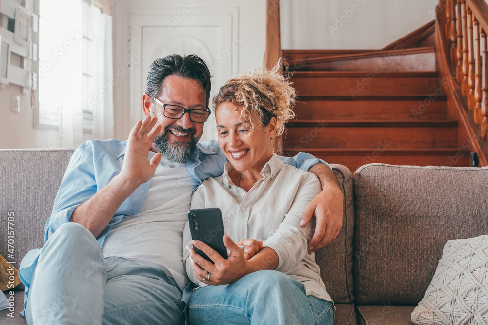 Happy caucasian couple resting on couch, waving hand in hello gesture ...