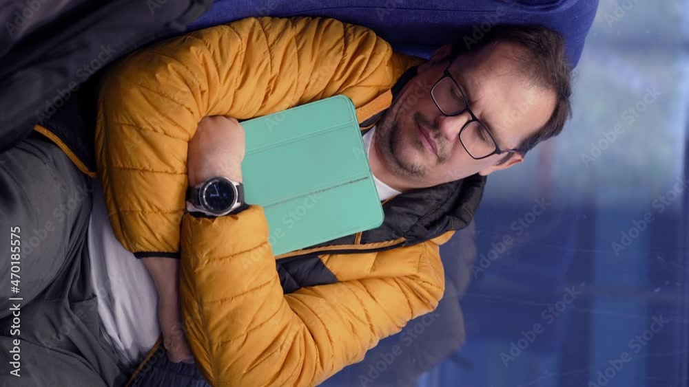 Tired millennial man in glasses and yellow jacket sitting by window on ...