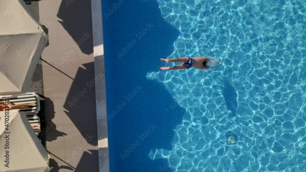 Top view of young man jumping in pool and splashing crystal clear water ...