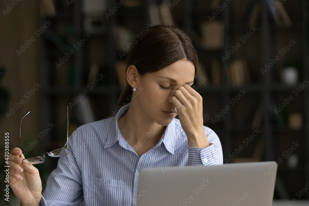 Tired young 30s businesswoman sit near laptop takes off glasses ...