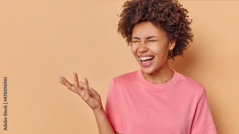 Joyful overemotive woman with curly hair gestures actively laughs out ...