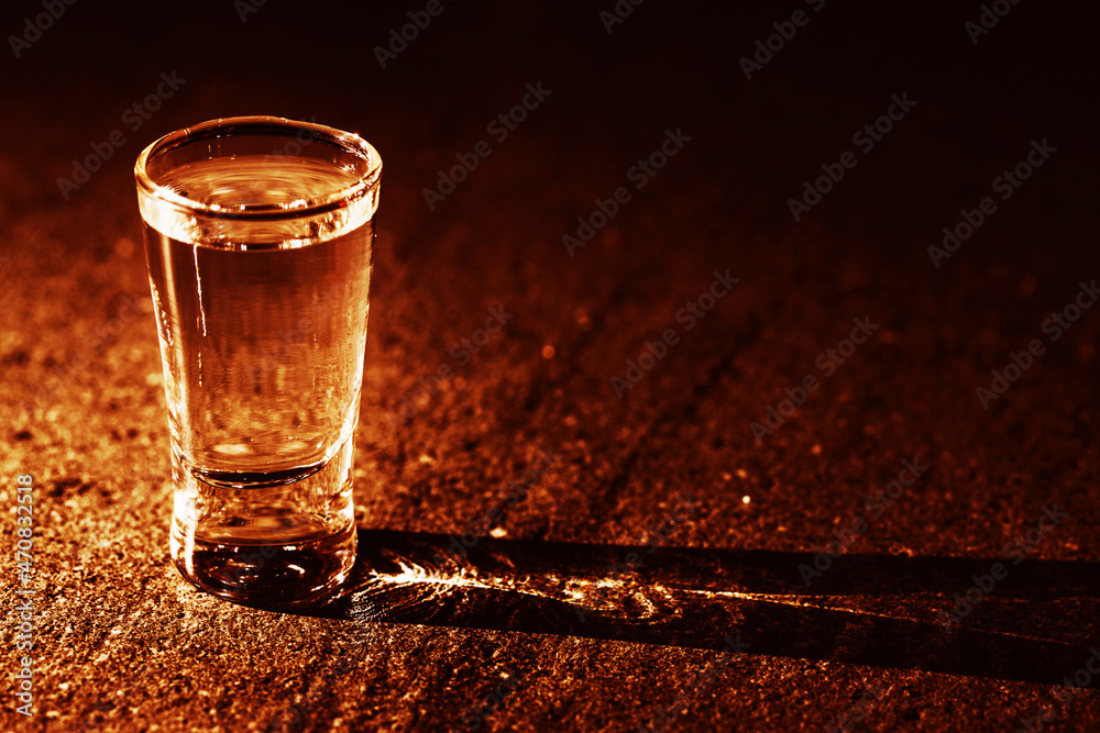 Transparent glass vodka shot on black bar. Empty copy space dark sad ...