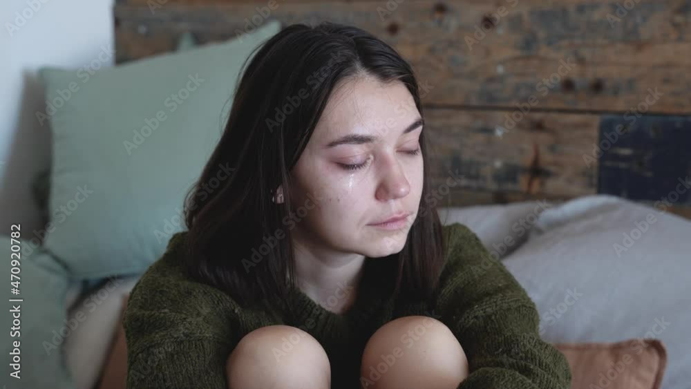 Sad frustrated caucasian young woman, sitting alone on the bed, in loft ...