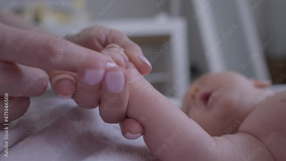Close-up female finger stroking newborn baby hand with blurred little ...