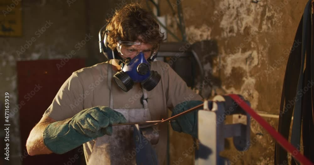 Caucasian male blacksmith wearing breathing mask and ear guards ...