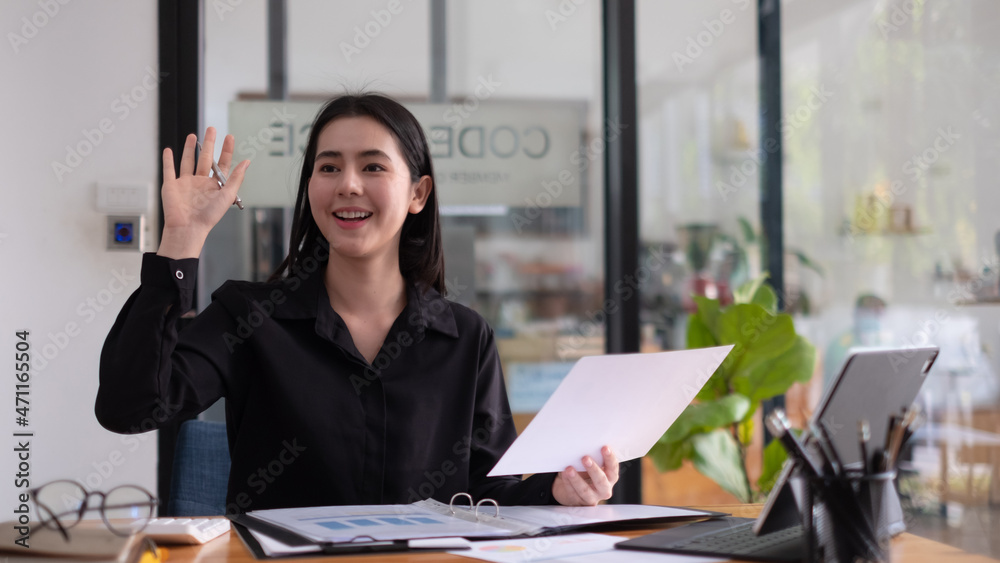 Friendly young business woman smiling and saying hi to her colleagues ...