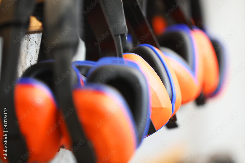 row of orange ear muffs ear protection on a rack. workplace health and ...