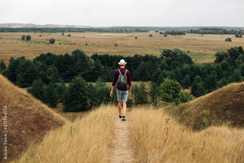 man with a backpack on a country walk on a summer day. Young people hiking in the countryside ...