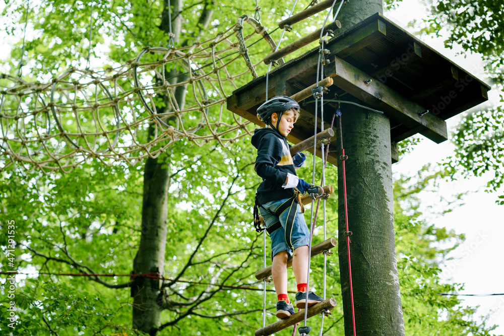 School boy in forest adventure park. Acitve child, kid in helmet climbs ...