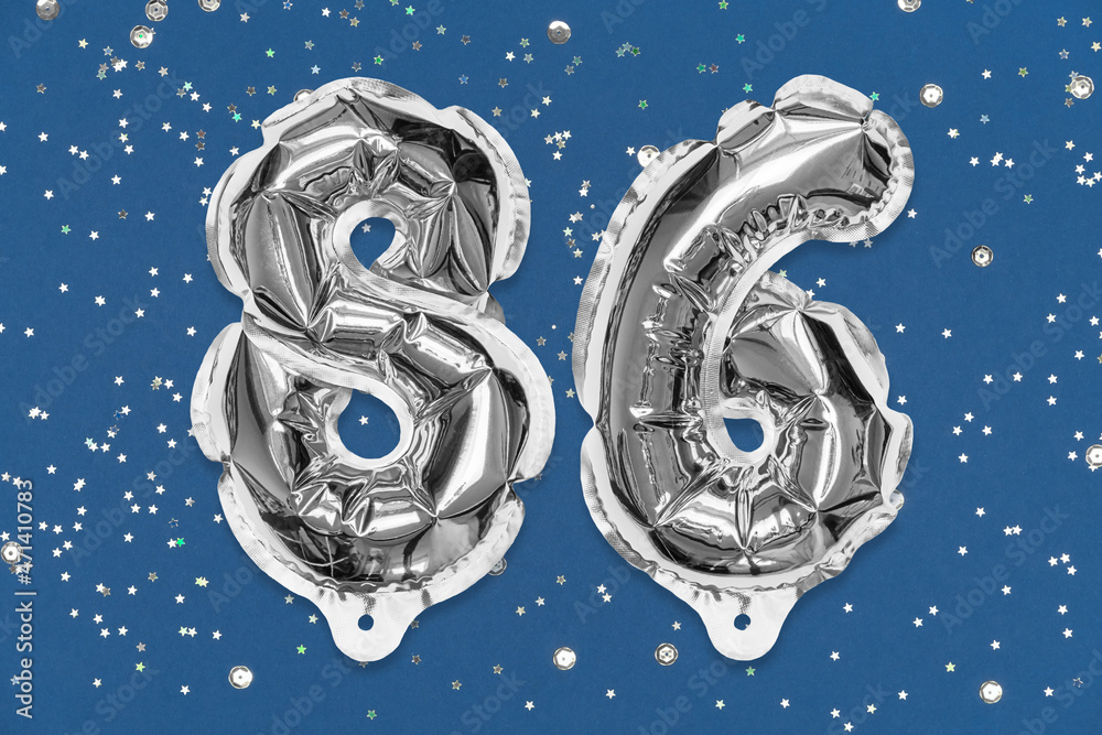 Silver foil balloon number, digit eighty six on a blue background with ...