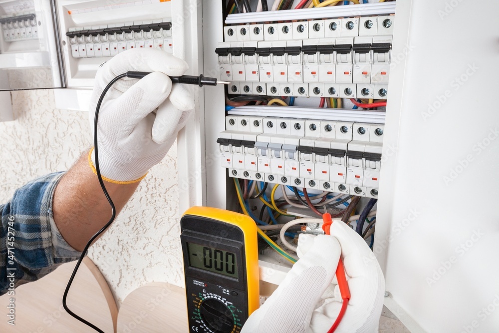 Electrician at work on an electrical panel protected in safety goggles ...