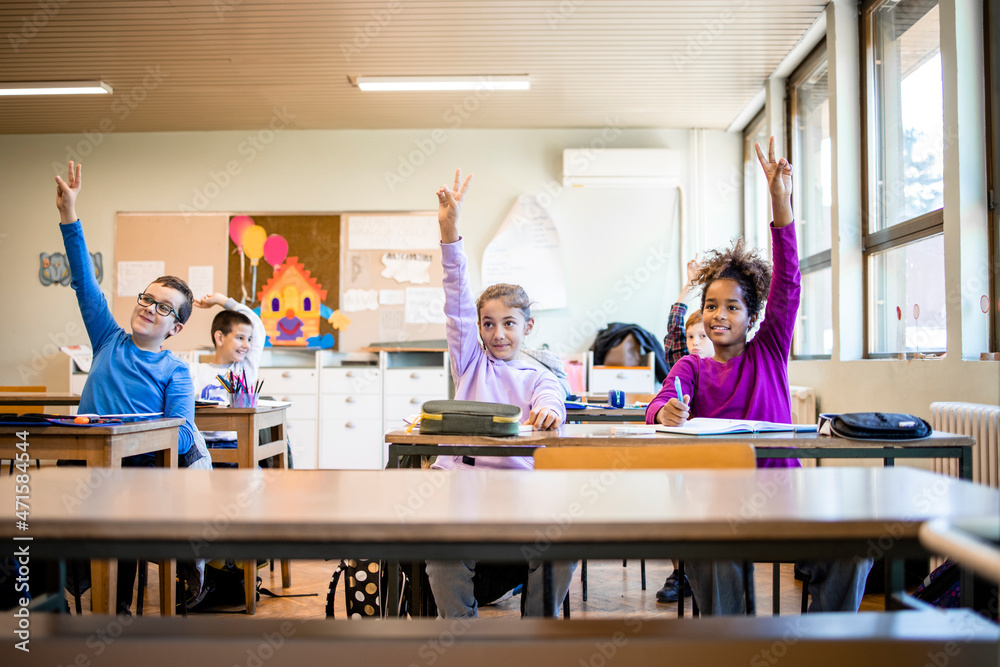 Schoolchildren at classroom with raised hands answering teacher's ...