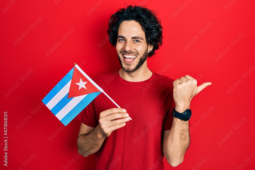 Handsome hispanic man holding cuba flag pointing thumb up to the side ...