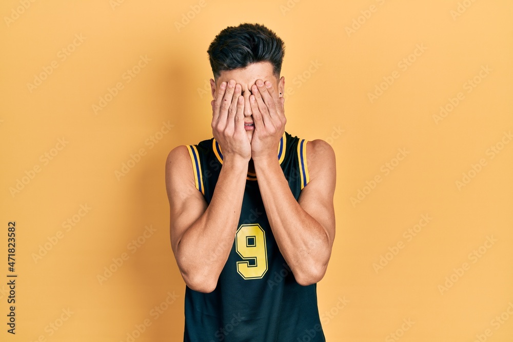 Young hispanic man wearing basketball uniform with sad expression ...