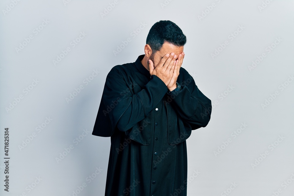 Handsome hispanic man with beard wearing catholic priest robe with sad ...