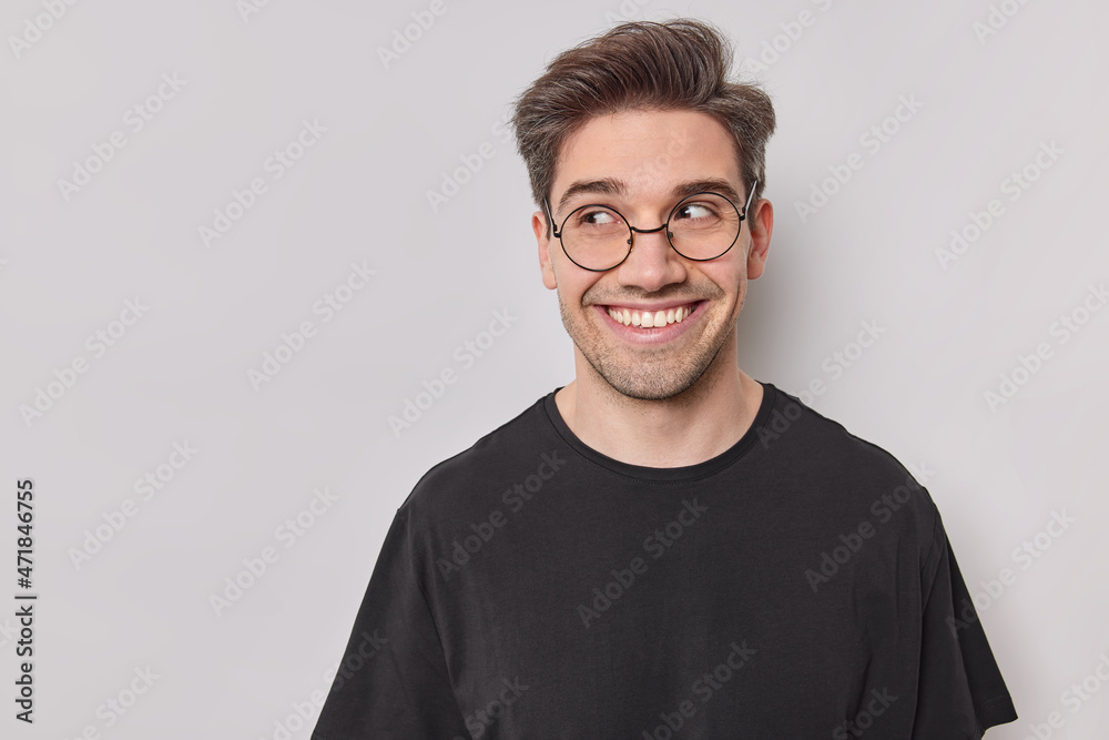 Portrait of handsome happy man looks curious aside wears round ...