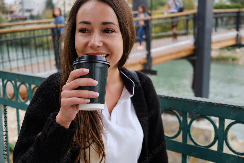 Smiling young adult caucasian woman drinks coffee on a walk at ...