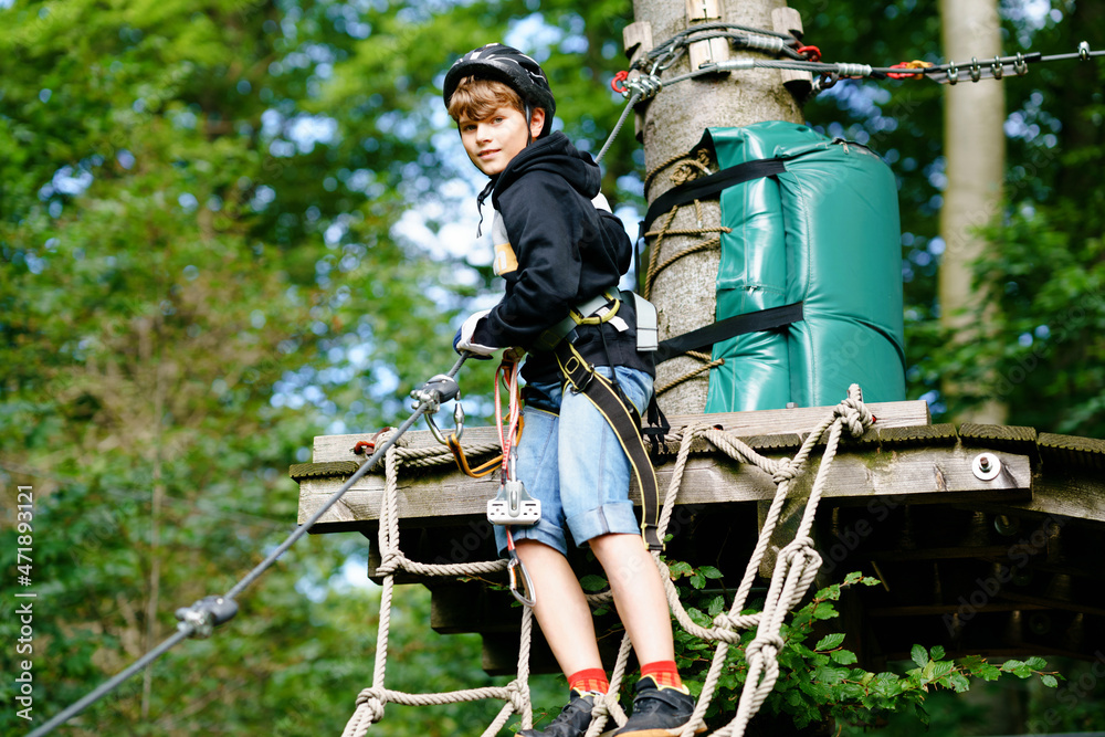 School boy in forest adventure park. Acitve child, kid in helmet climbs ...
