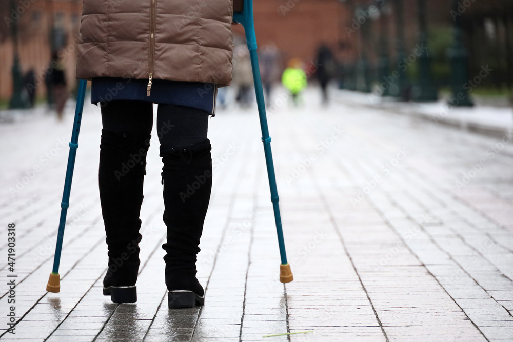 Woman walking with crutches on a city street on people background ...