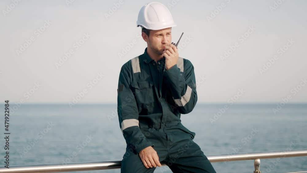 Young port worker in helmet and coverall using vhf radio, controlling ...
