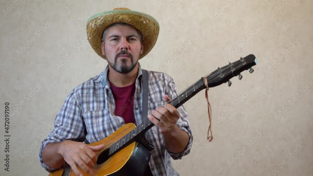 The man plays the guitar and sings. On his head is a straw hat ...