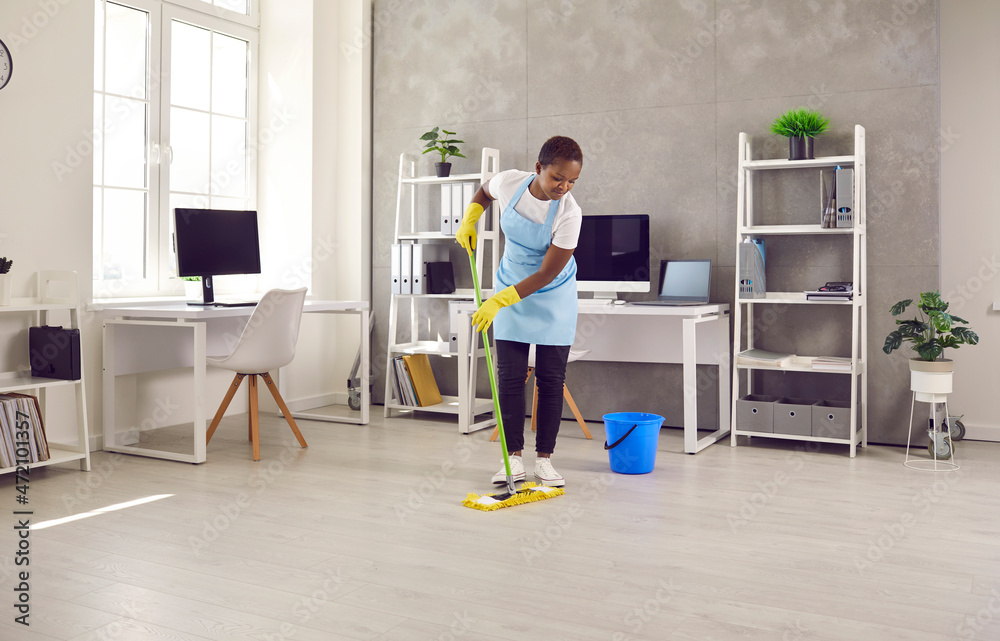 Foto de African American woman janitor with mop clean office floor with ...