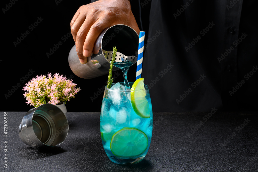 bartender serving with a cocktail shaker a blue drink in a glass ...