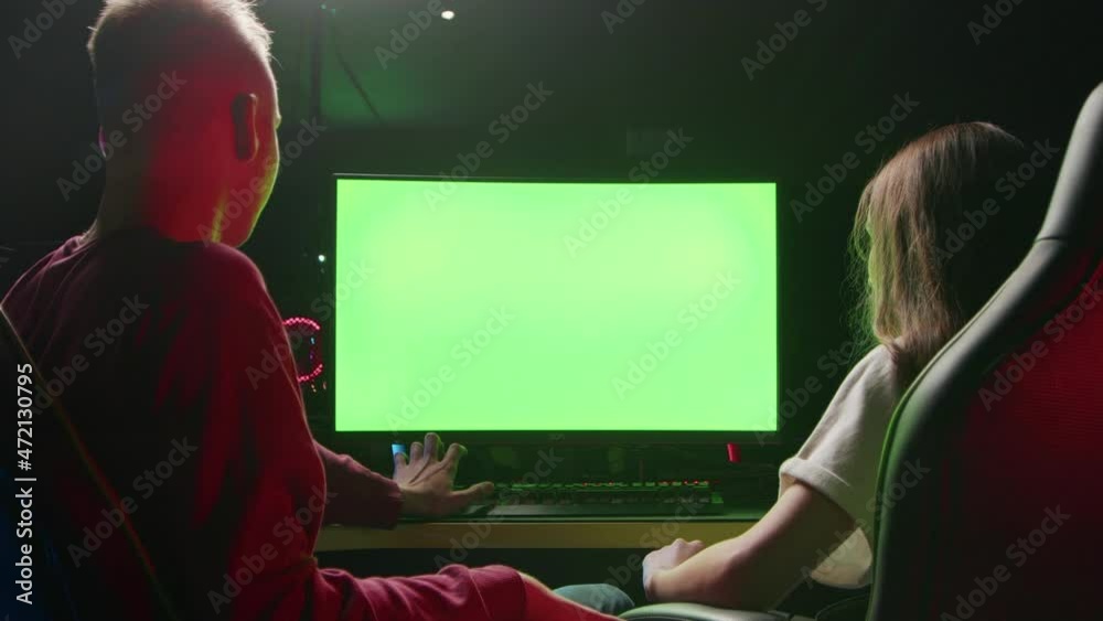 A guy and a girl are sitting at a computer and looking at a green ...