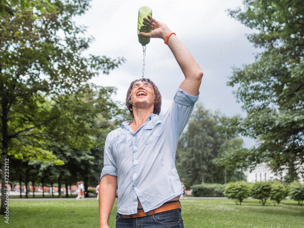 Laughing man douses himself with water from bottle. Staying cool in ...