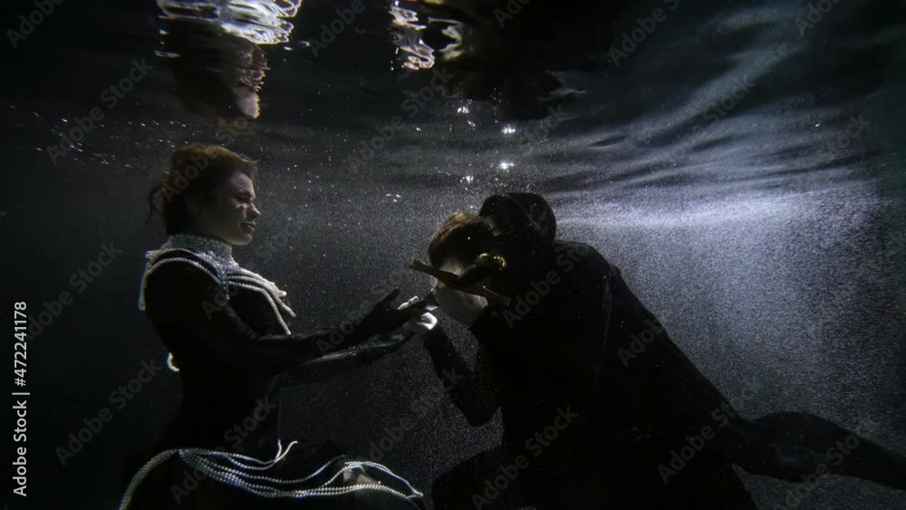 Underwater performance an imperious woman hands a large sword to a ...