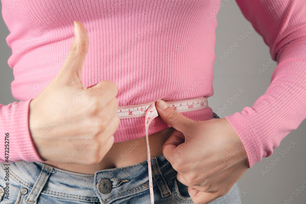 Young woman measuring abdominal circumference with tape measure and ...