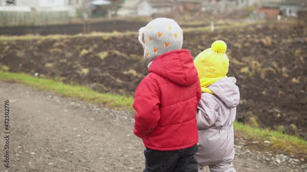 baby runing.Two little kids in grey jumpsuit yellow hat walking through ...