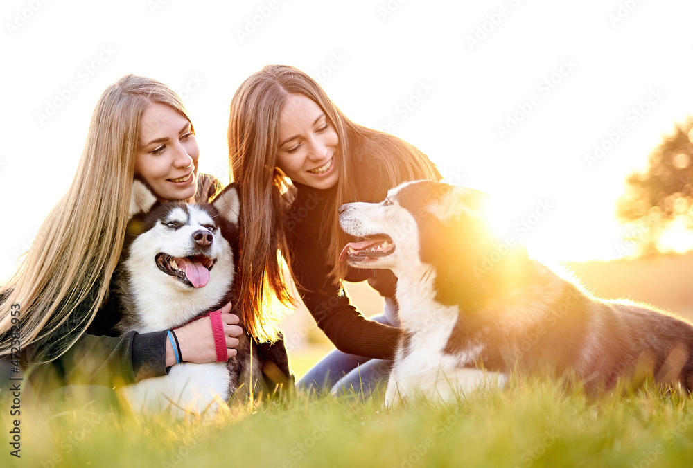 Millennial girls playing with their siberian husky dogs outdoors ...