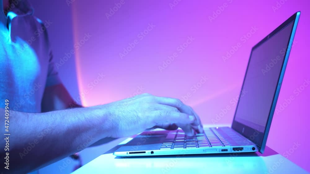 Man Works at a Laptop, Typing Text on the Keyboard. Indoors Neon Lighting and a Futuristic ...
