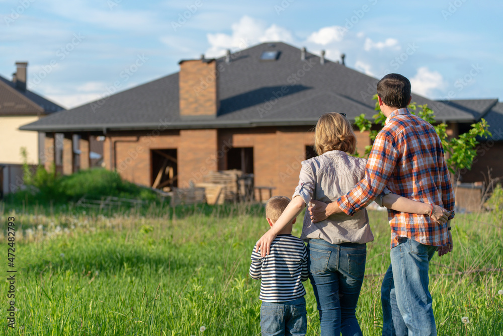 Back view of happy family is standing near their new modern house and ...
