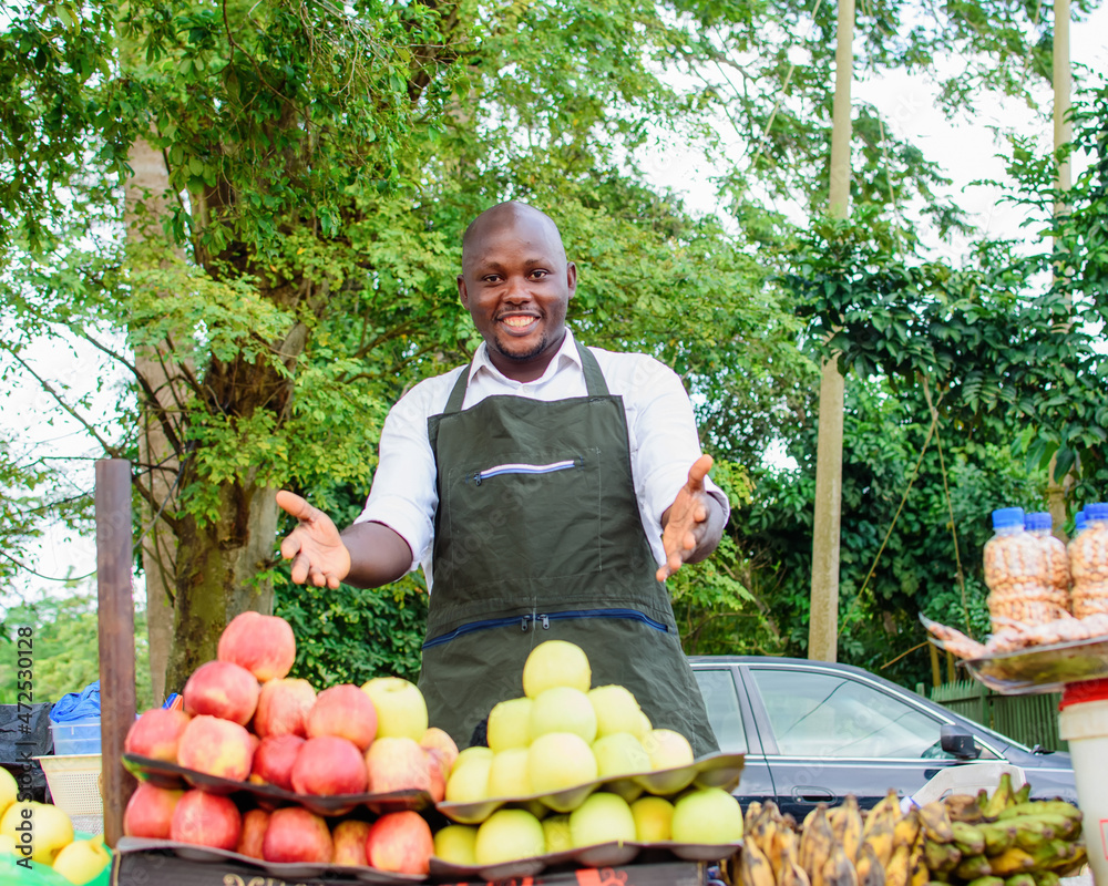 Happy African male trader or vendor standing at his fruit stall in a ...