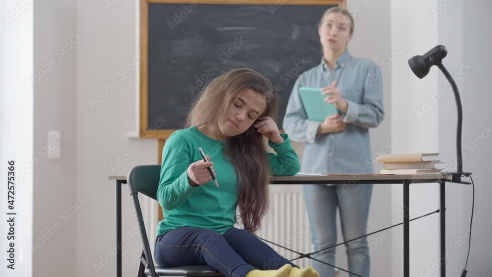Bored little person sitting on chair at desk in classroom playing with ...