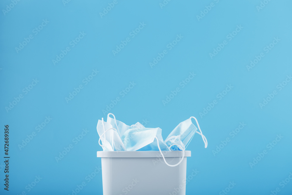 Waste bin full of used protective masks on a light blue background with ...