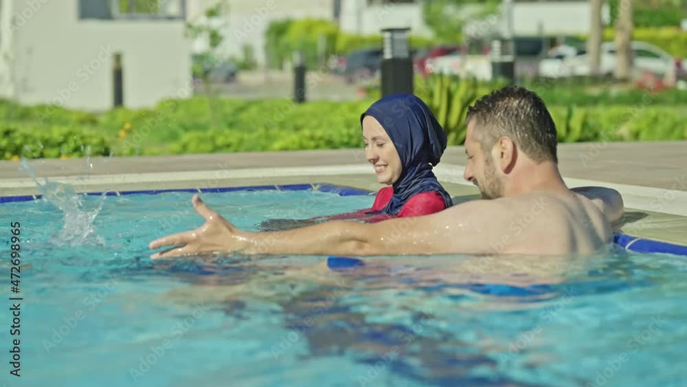 A young woman wearing a hijab swimsuit is swimming in the pool with her ...