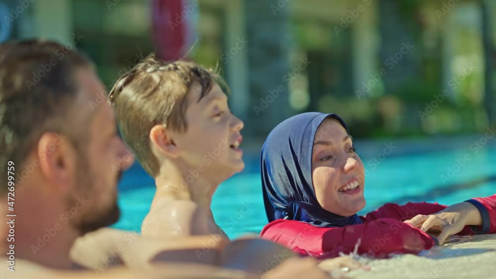 A young woman wearing a hijab swimsuit is swimming in the pool with her ...