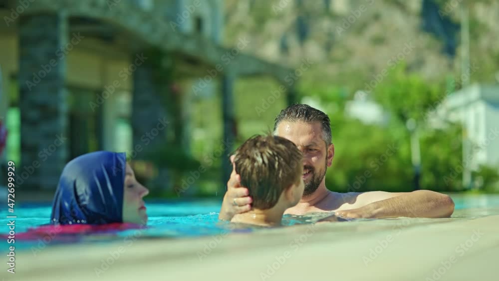 A young woman wearing a hijab swimsuit is swimming in the pool with her ...