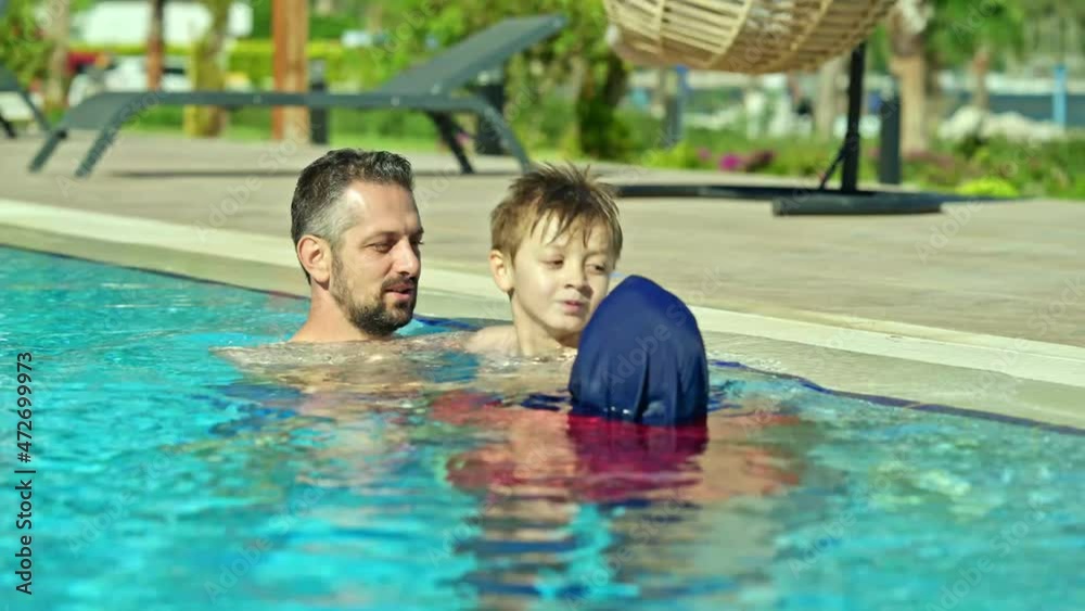 A young woman wearing a hijab swimsuit is swimming in the pool with her ...
